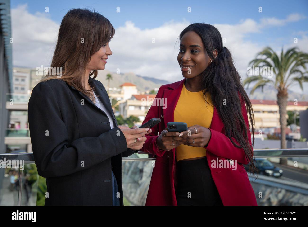Two business women use smartphones and have a conversation at work ...