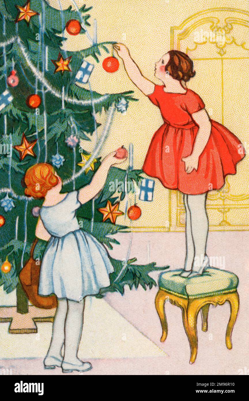Two girls, one standing on a stool, decorate their Christmas tree with ...