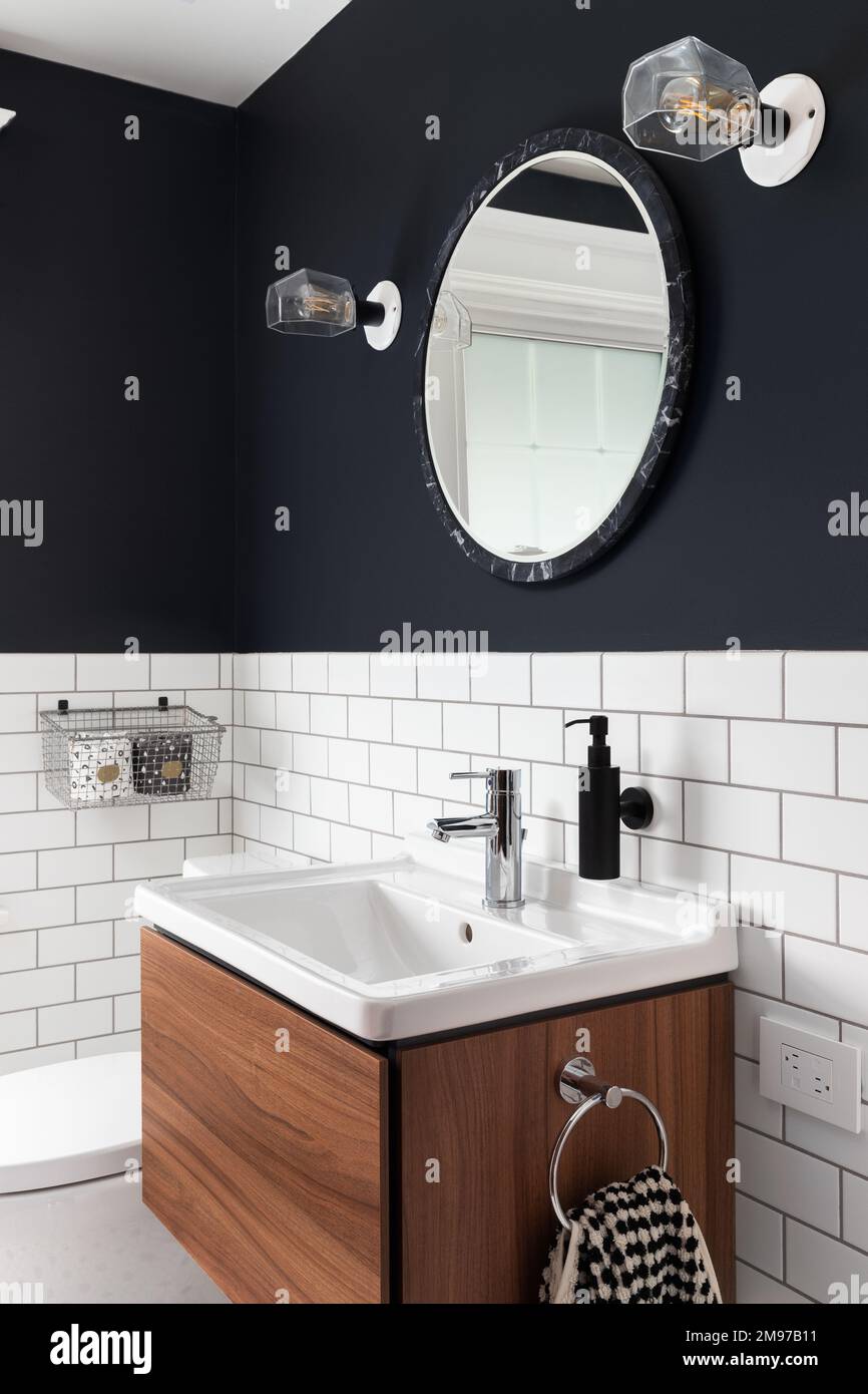 A bathroom detail with dark blue walls, subway tiles, sconces around a ...