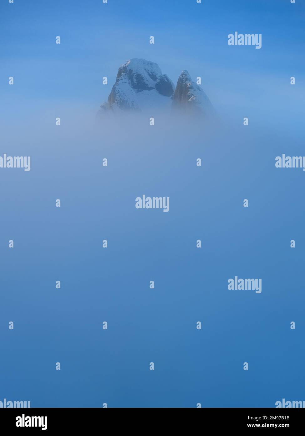 Aerial view of distant mountain peaks above clouds in clear sunny blue ...