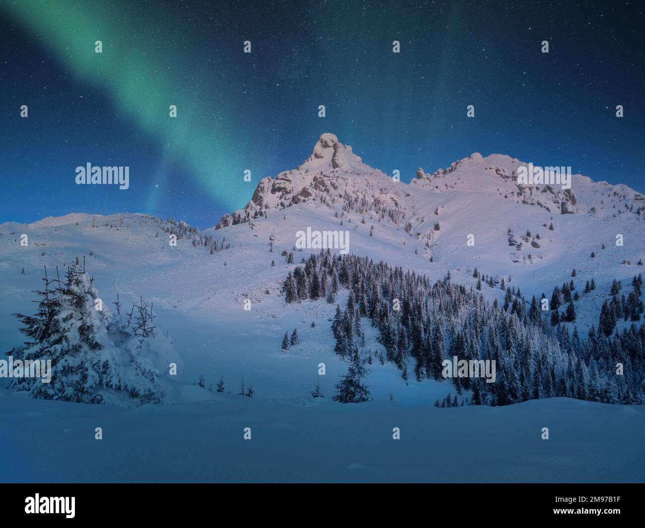 Aurora Borealis appear over a snow covered mountain in winter landscape ...