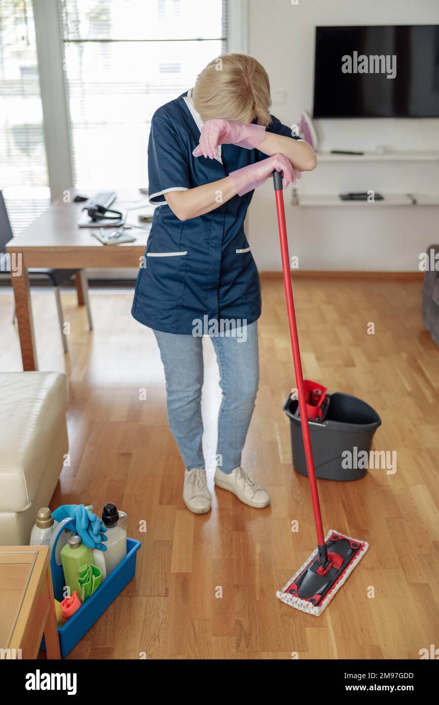 Tired housemaid in uniform washing floor and bend over mop in living ...