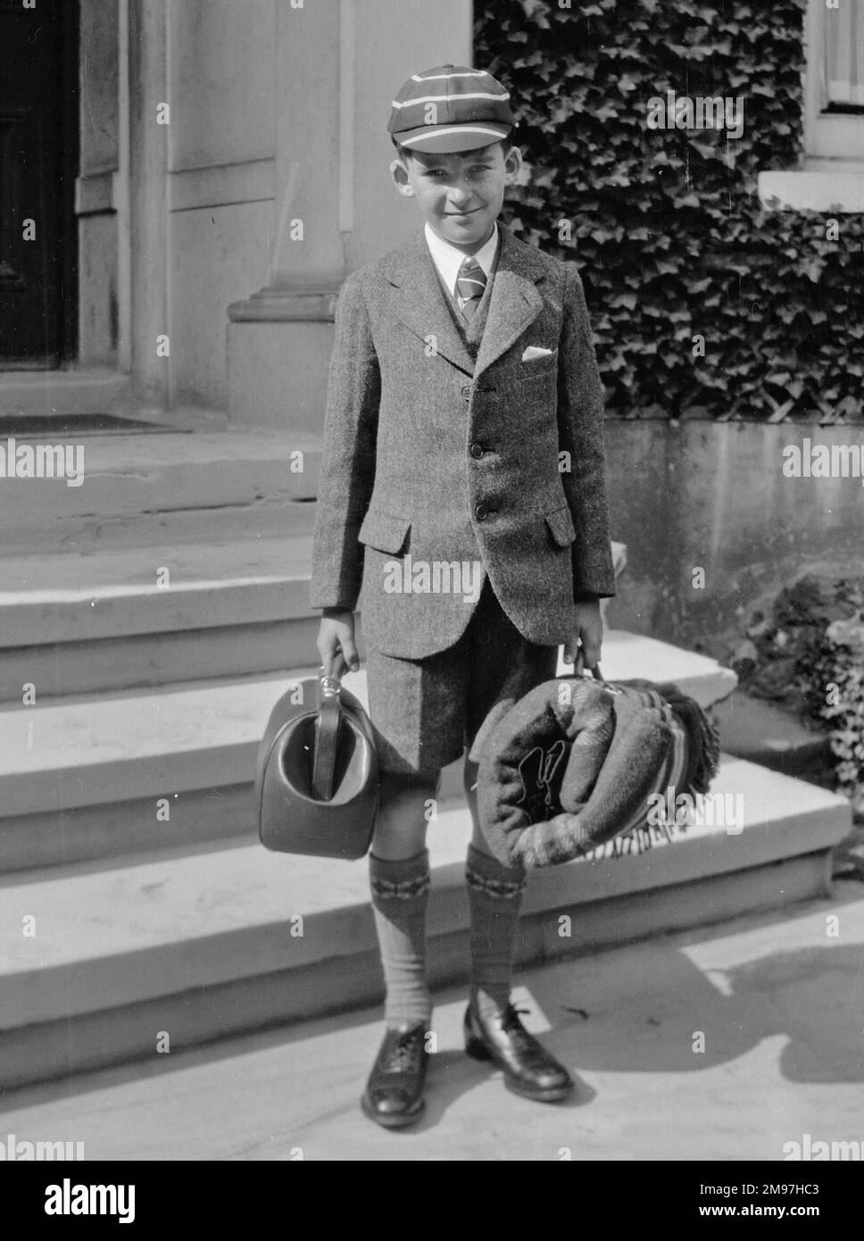 A boy in school uniform with luggage -- a bag and a rolled up blanket ...