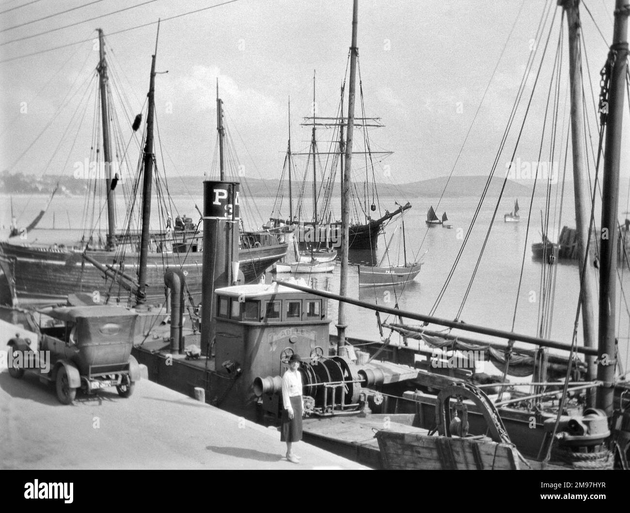 Ships and boats in a harbour, with a woman standing on the quay near a ...