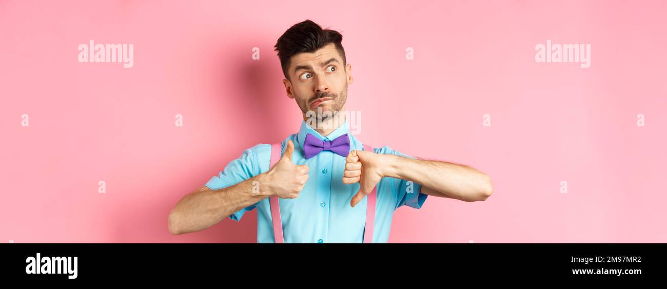 Confused guy looking pensive while judging, showing thumbs up and down ...