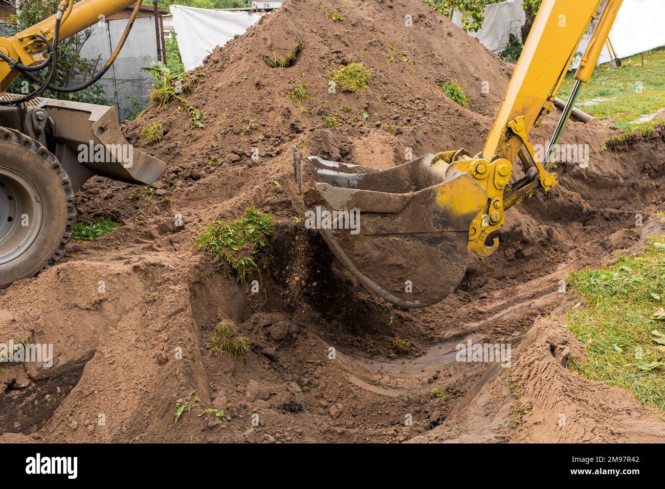 A bucket of excavator or bulldozer with a pile of earth digs a hole on ...