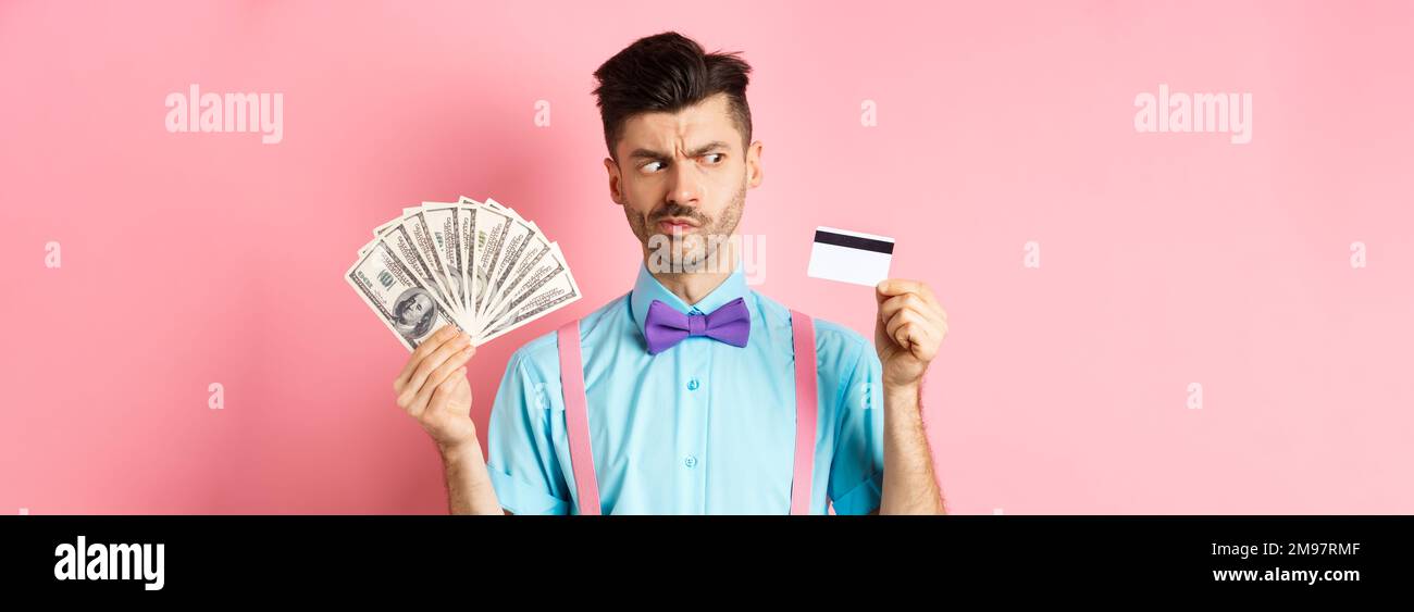 Doubtful and indecisive guy looking hesitant at plastic credit card ...