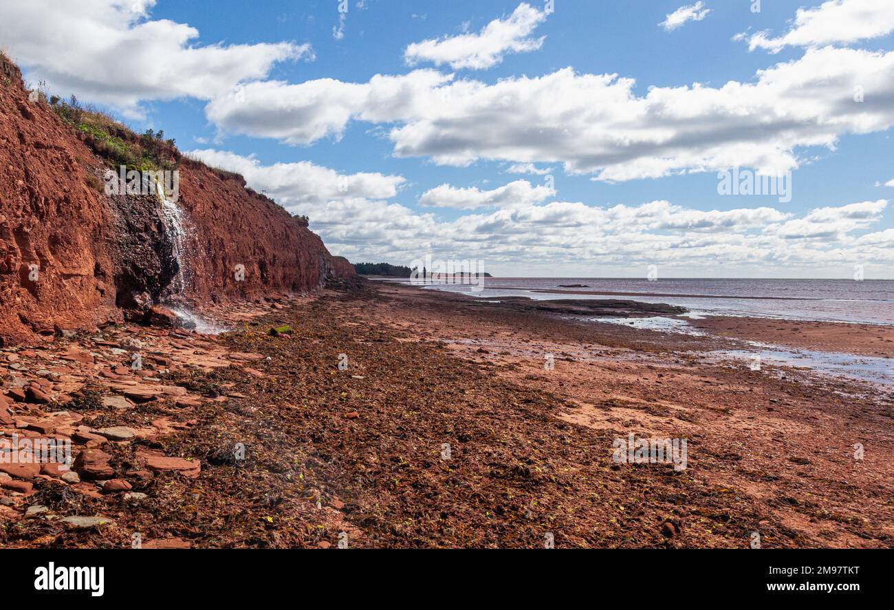 Water pouring over the edge of a cliff onto red clay beach, Prince Edward Island, Canada Stock ...