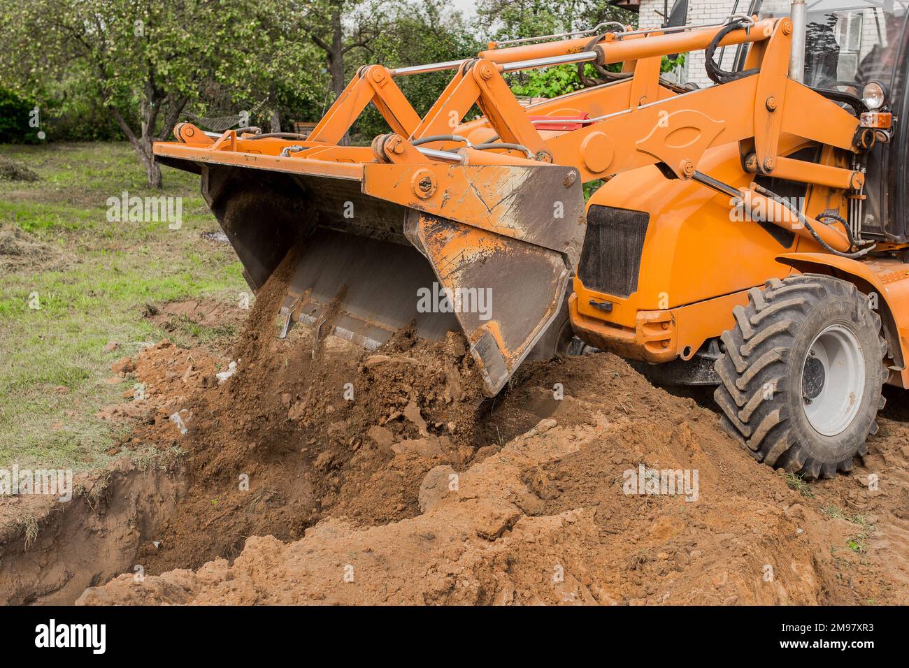 A bucket of a bulldozer fills the trench with earth in an industrial ...