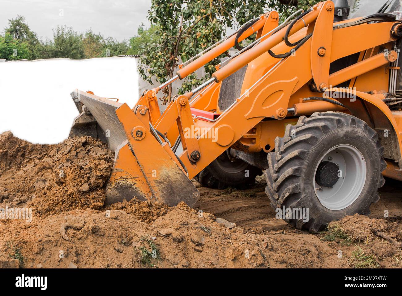 A bucket of a bulldozer fills the trench with earth in an industrial ...