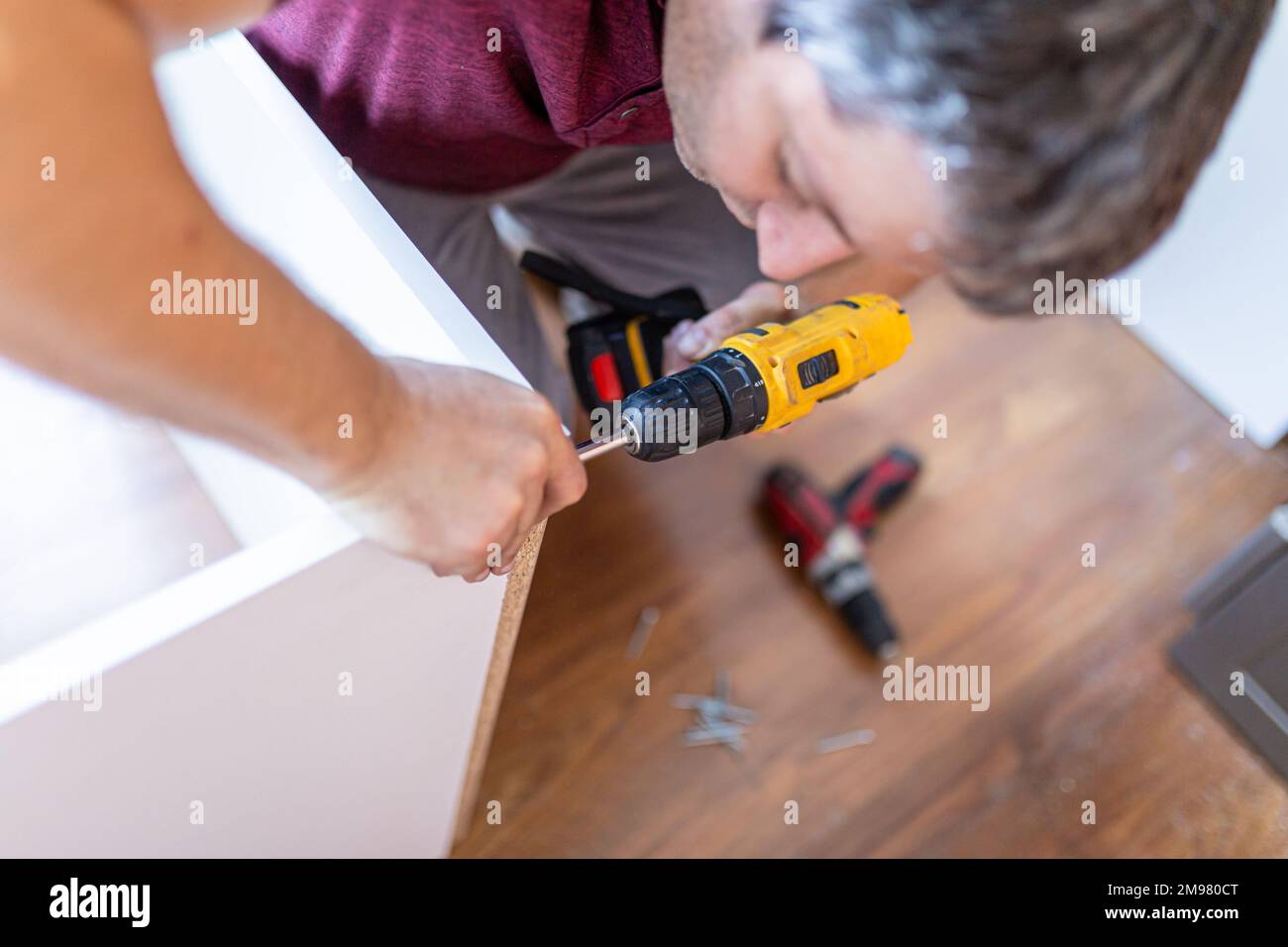 Handyman at work. Repairing kitchen shelves with cordless screwdriver ...