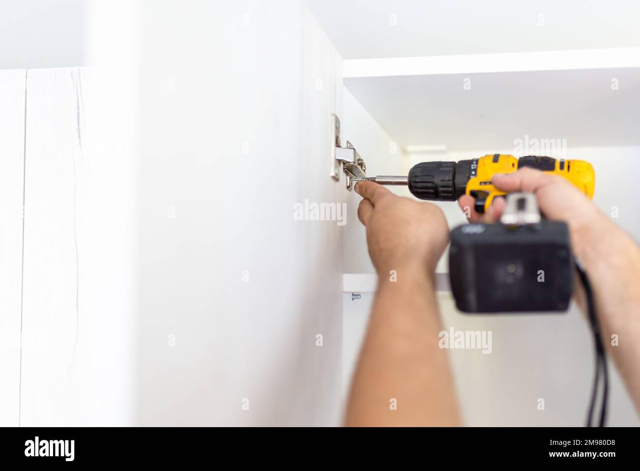 Handyman using screwdriver while installing kitchen cabinets at home ...
