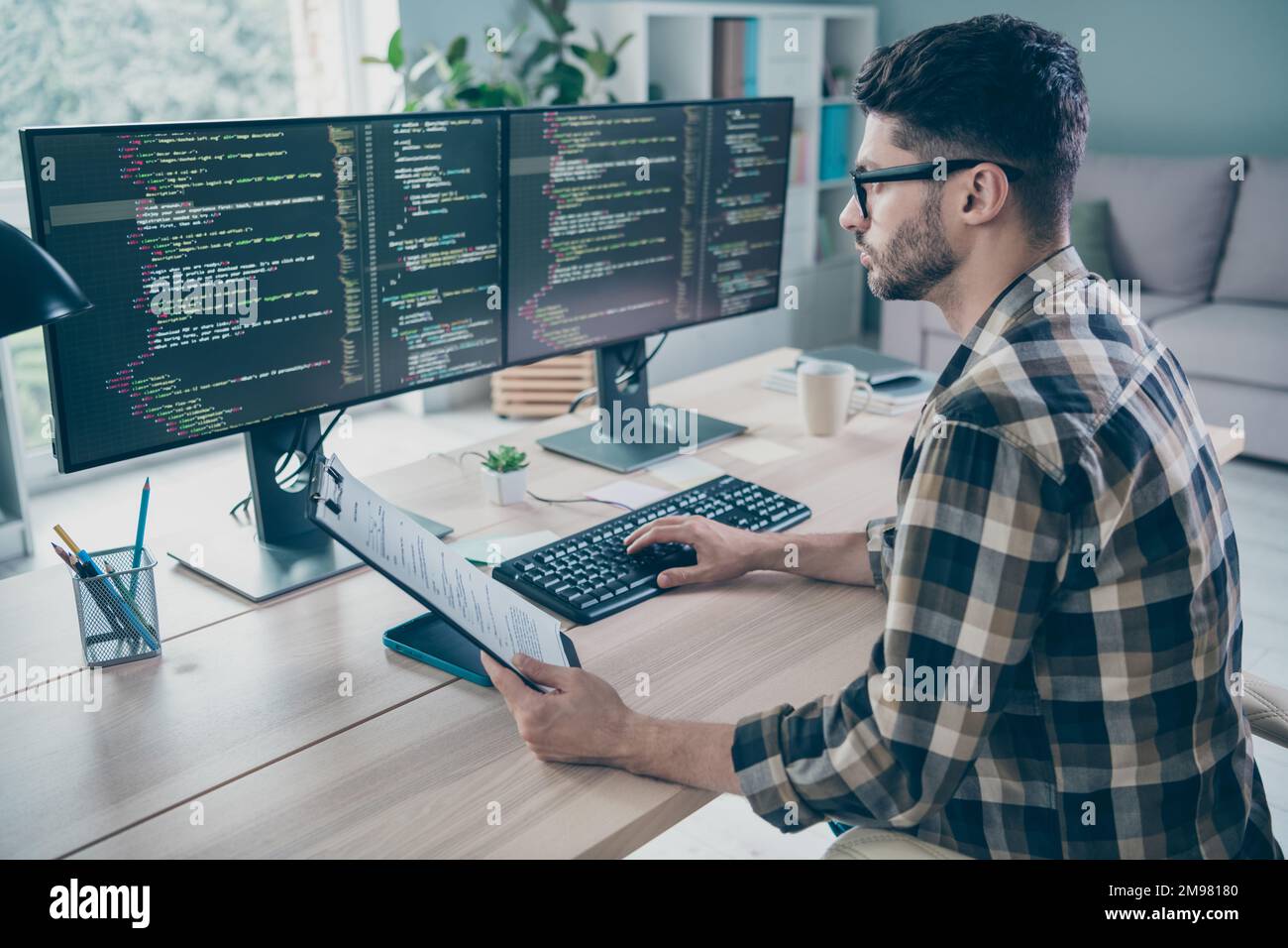 Photo of serious busy coder dressed eyewear holding list typing modern ...