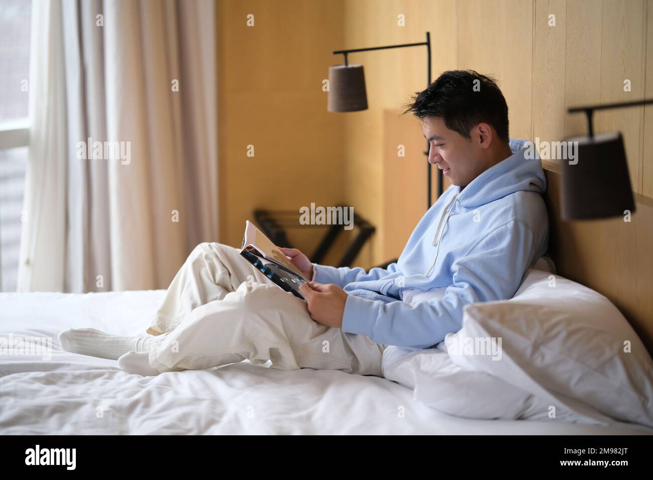 handsome Asian young man read magazine on bed. Side view Stock Photo - Alamy