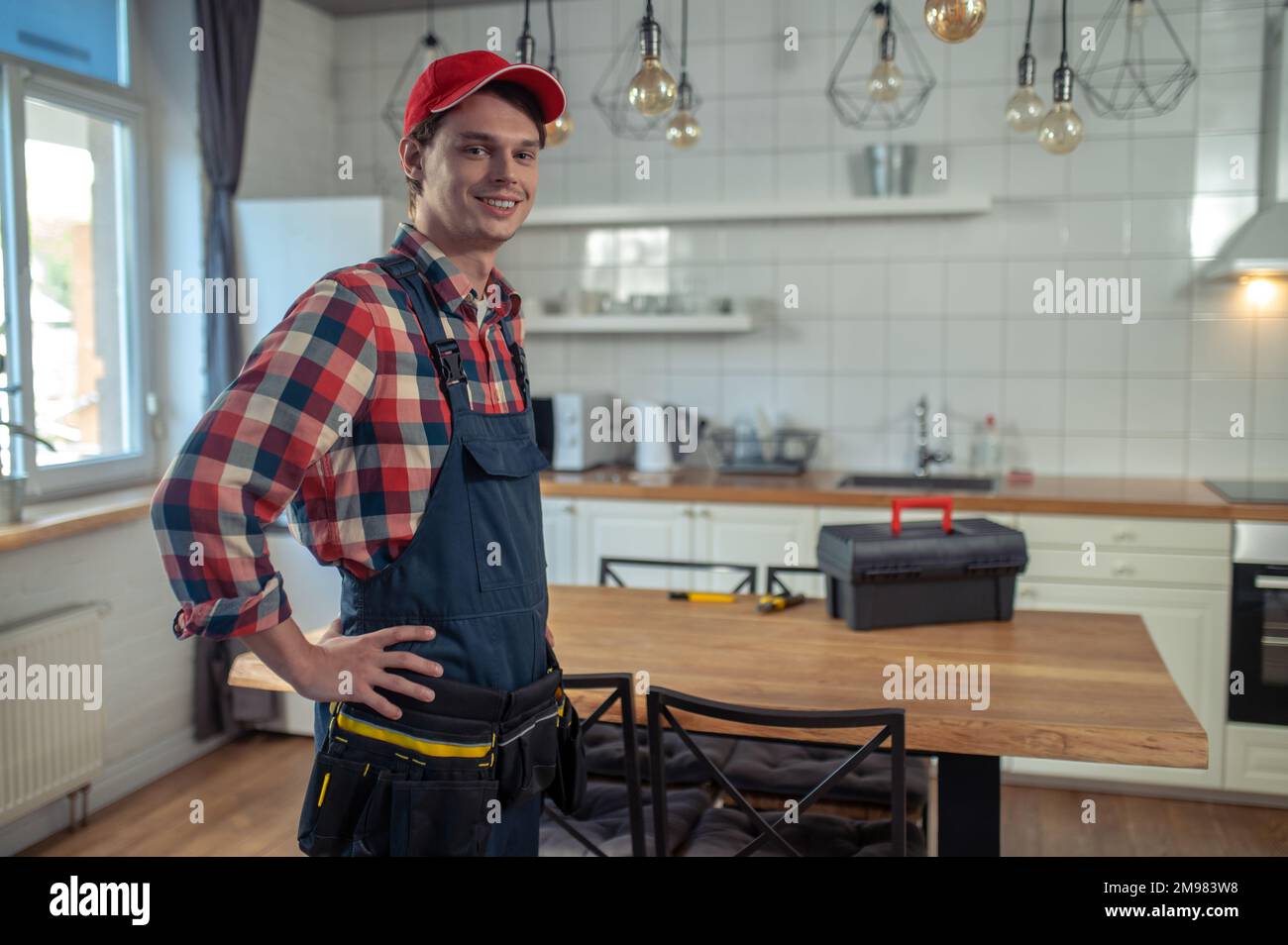 Smiling happy serviceman dressed in the tool belt and overalls standing ...