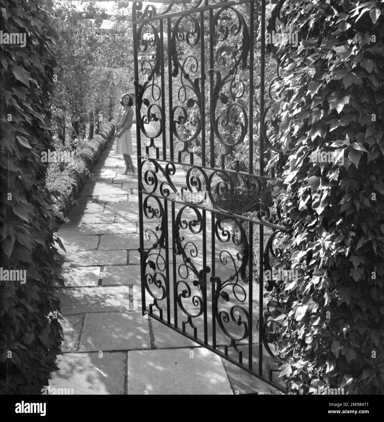 Wrought iron gate in a garden with female model on the path in the ...