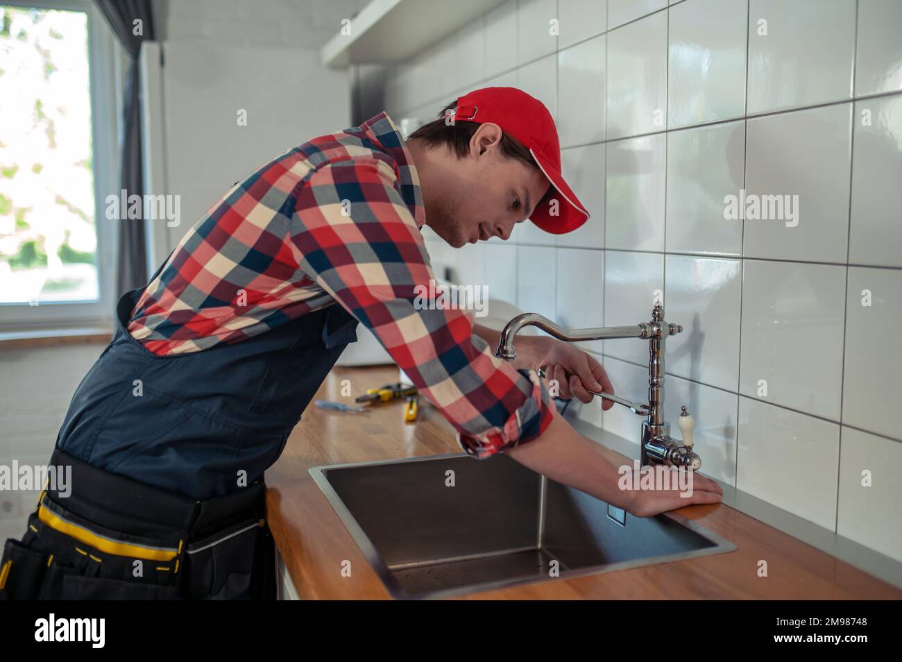 Side view of a focused plumber tightening the screw on the faucet with ...