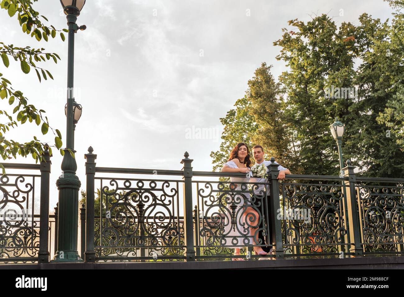 Beautiful happy married couple stands in the summer on retro bridge and ...