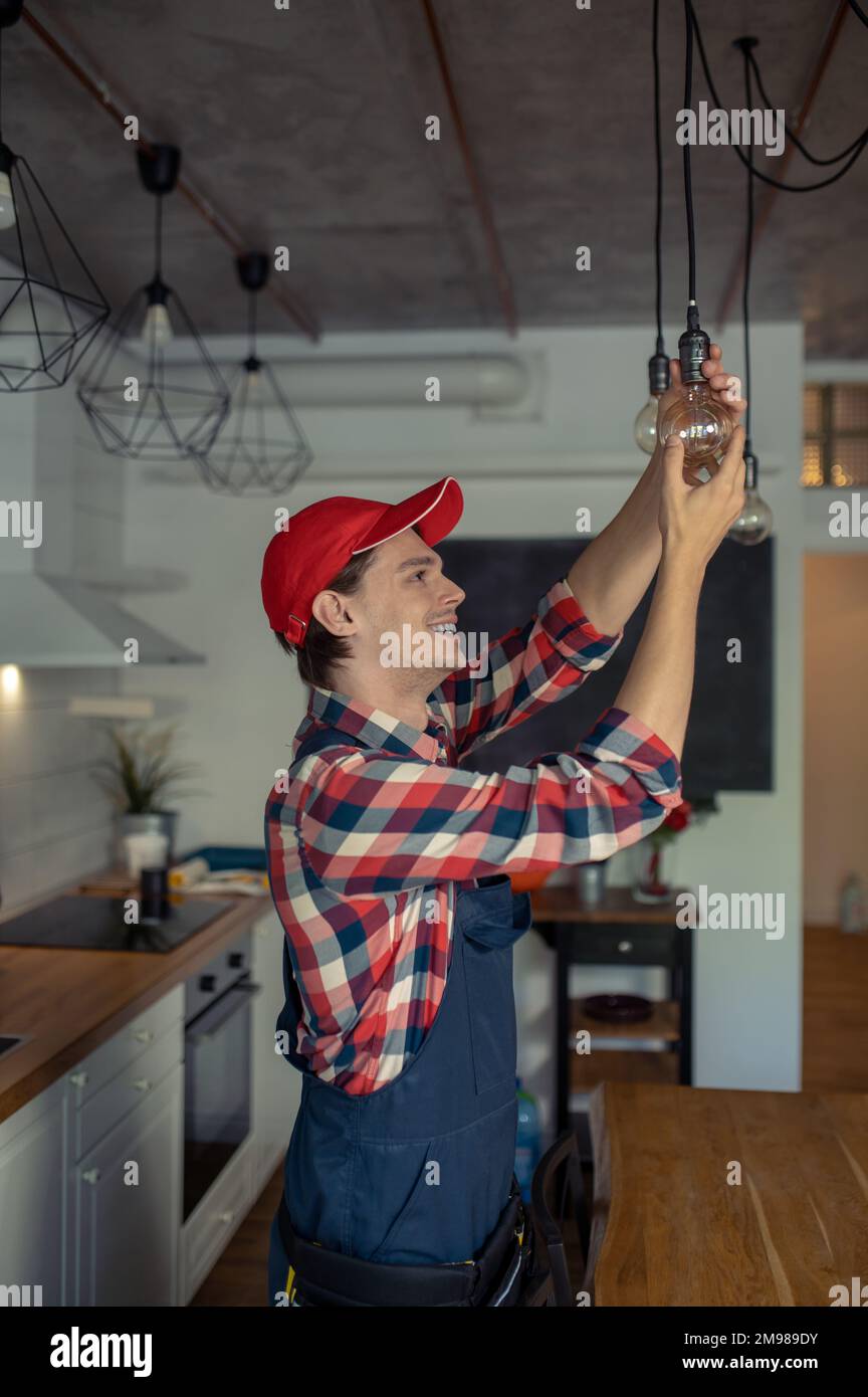 Side view of a smiling joyful electrical technician screwing the light ...