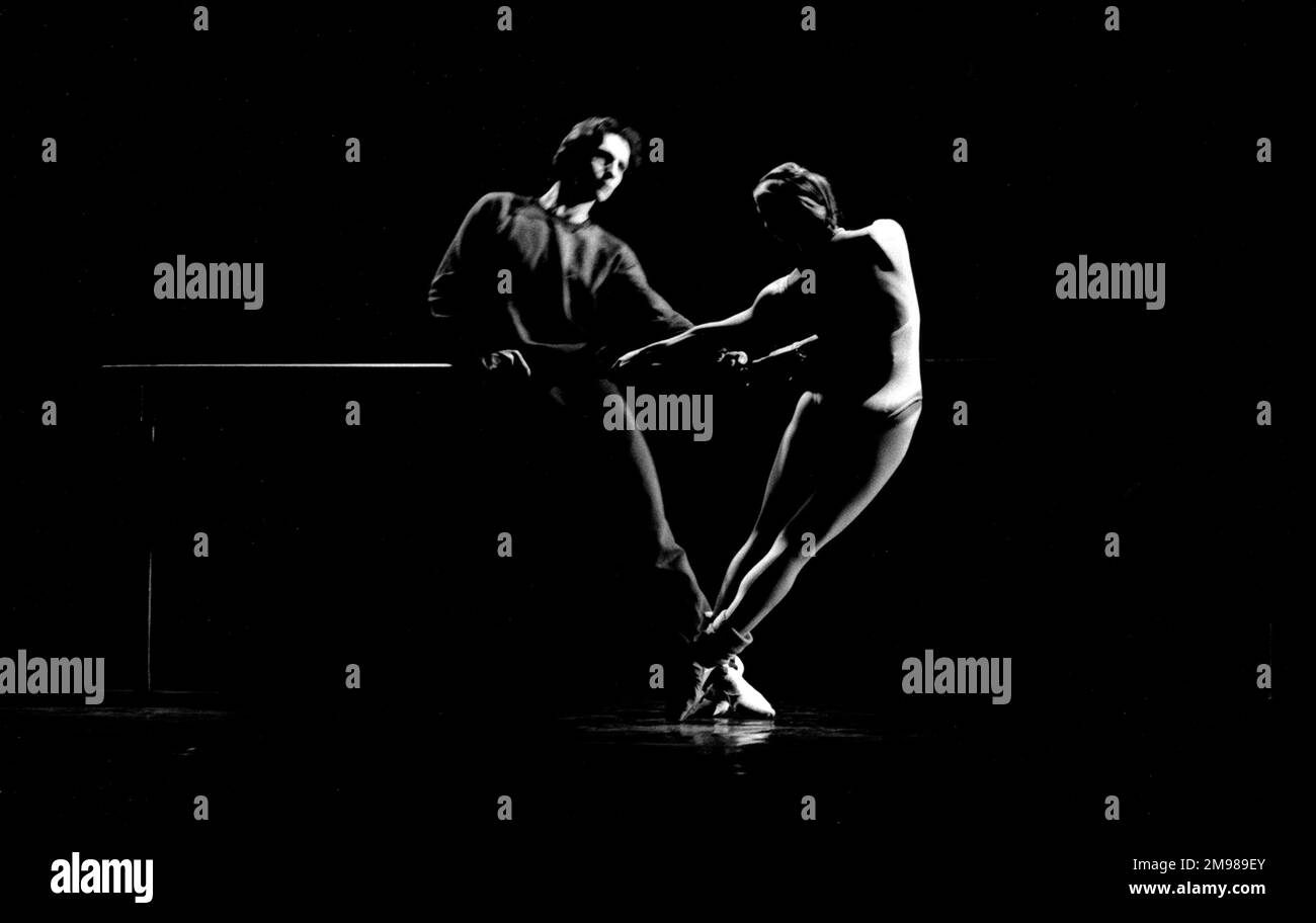 Two ballet dancers in a dark setting, male and female, at the barre ...