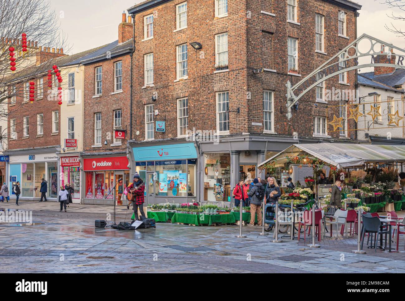 A pedestrian shopping street with a market flower stall and the tables ...