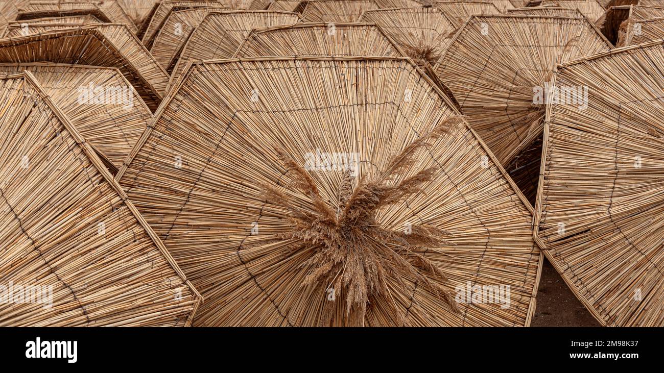 Straw beach umbrellas are stacked Stock Photo - Alamy