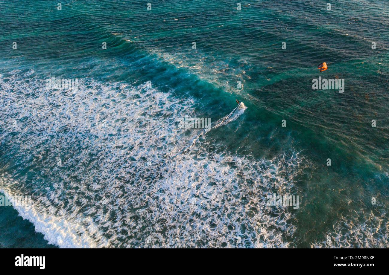 Aerial shot over blue coral reef bay wide waves with kiteboarder riding ...