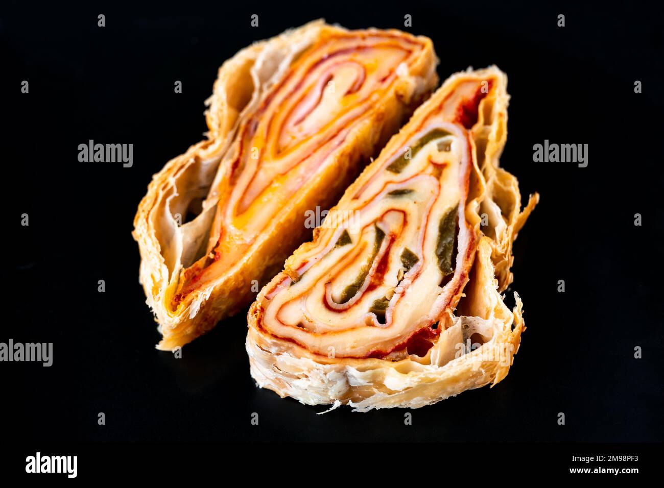 Two piece of sliced salty rolled pastry with ham, cheese and jalapenos ...