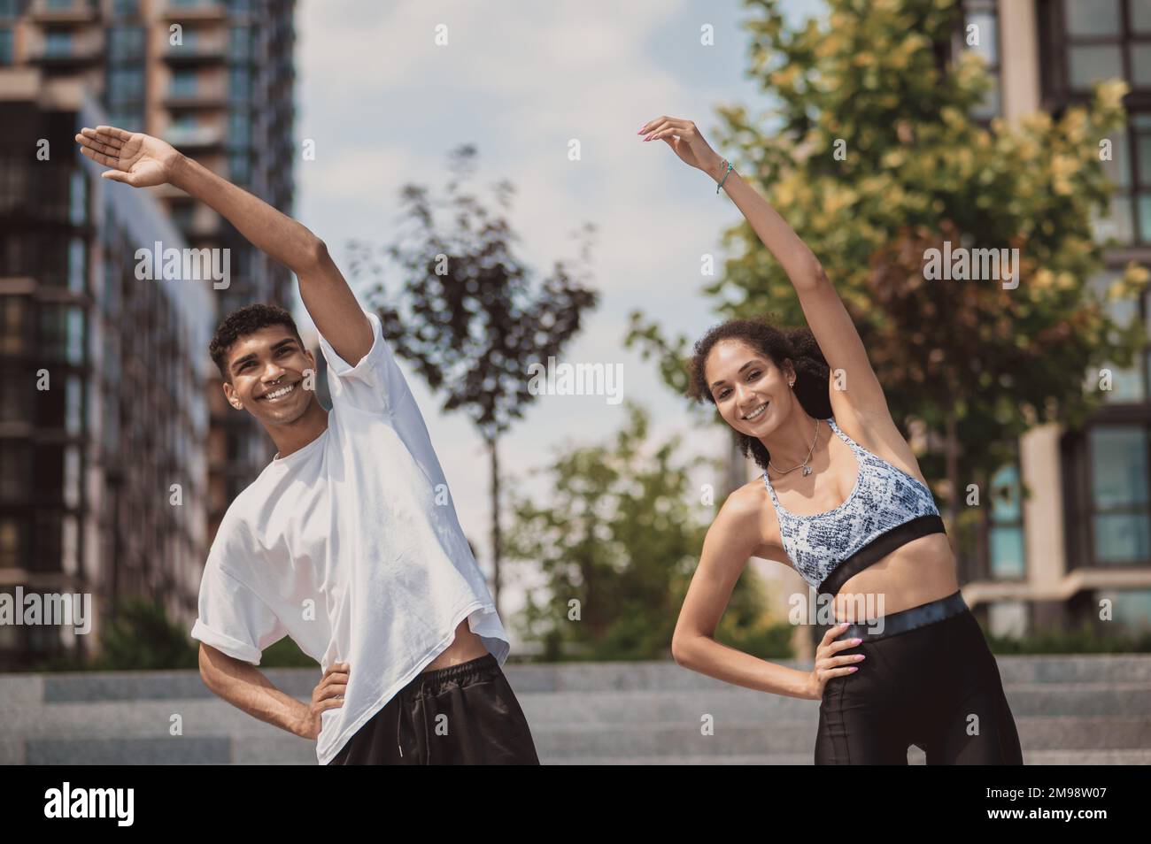 Two joyous athletes doing side bends outdoors Stock Photo - Alamy