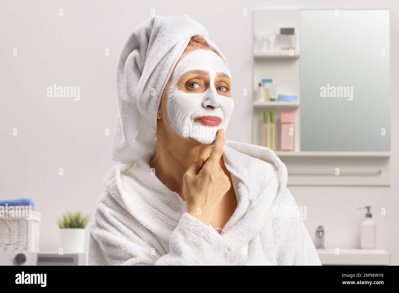 Happy mature woman with a white face mask posing inside a bathroom ...