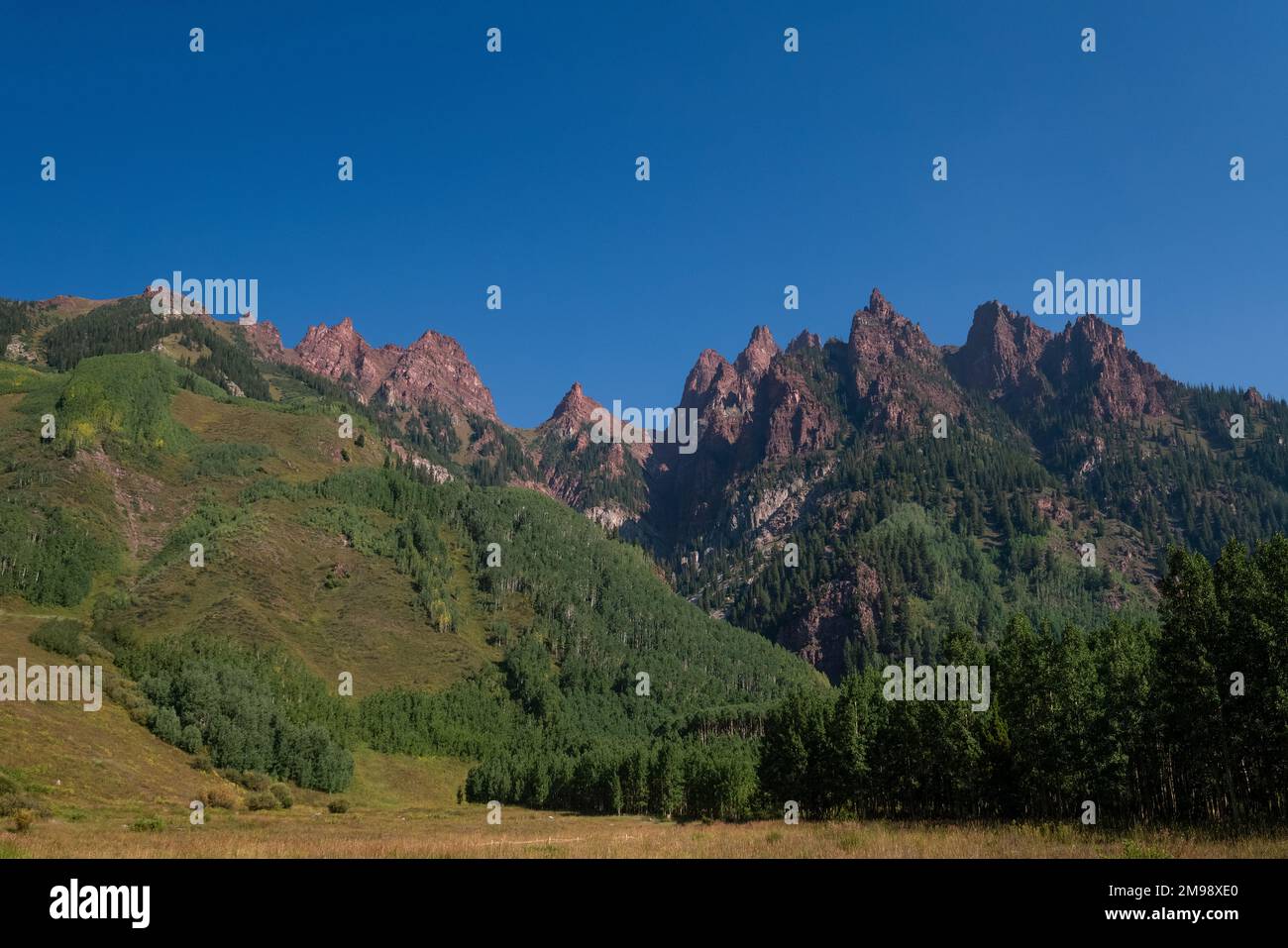 An image of mountains with red tops behind the green range of trees ...