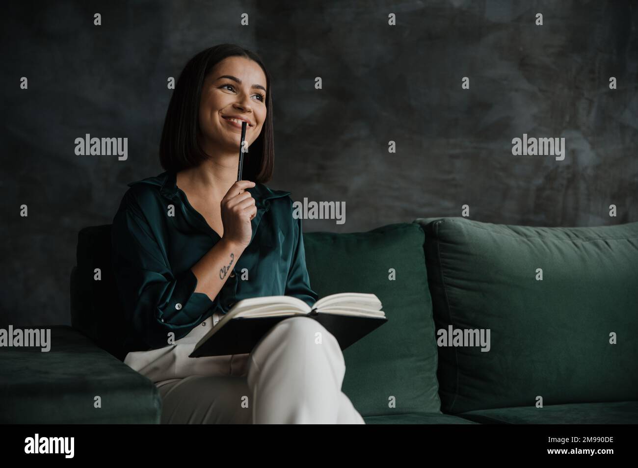 Serious woman sitting on green couch in loft living room, working from ...