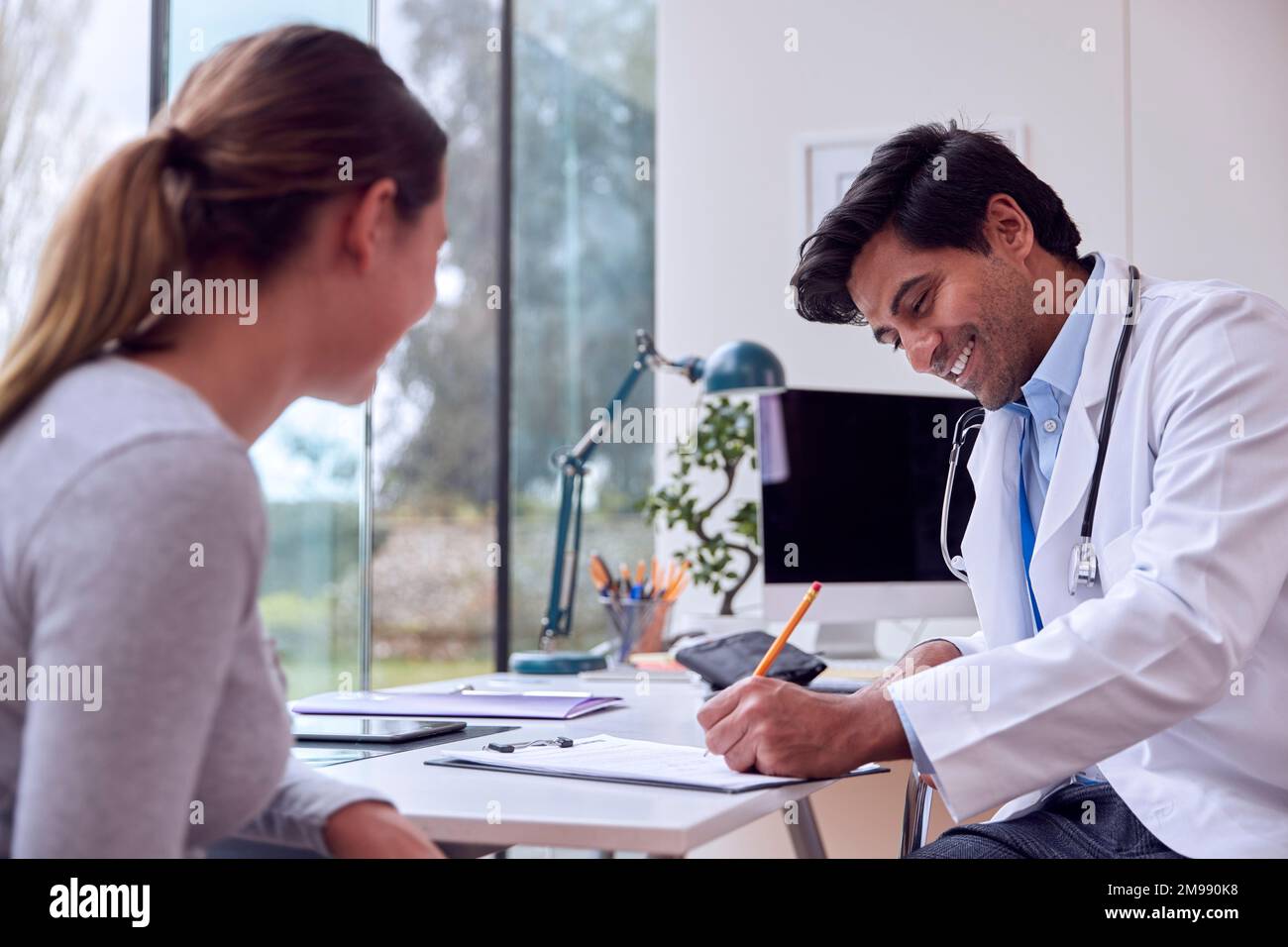 Male Doctor Or GP In Appointment With Teenage Girl Making Notes On ...