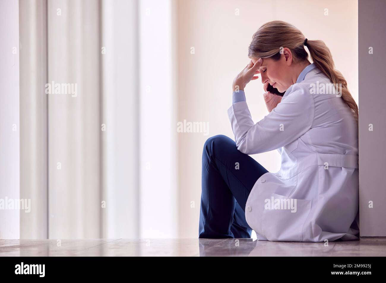 Stressed Female Doctor Wearing White Coat Sitting On Floor In Hospital ...
