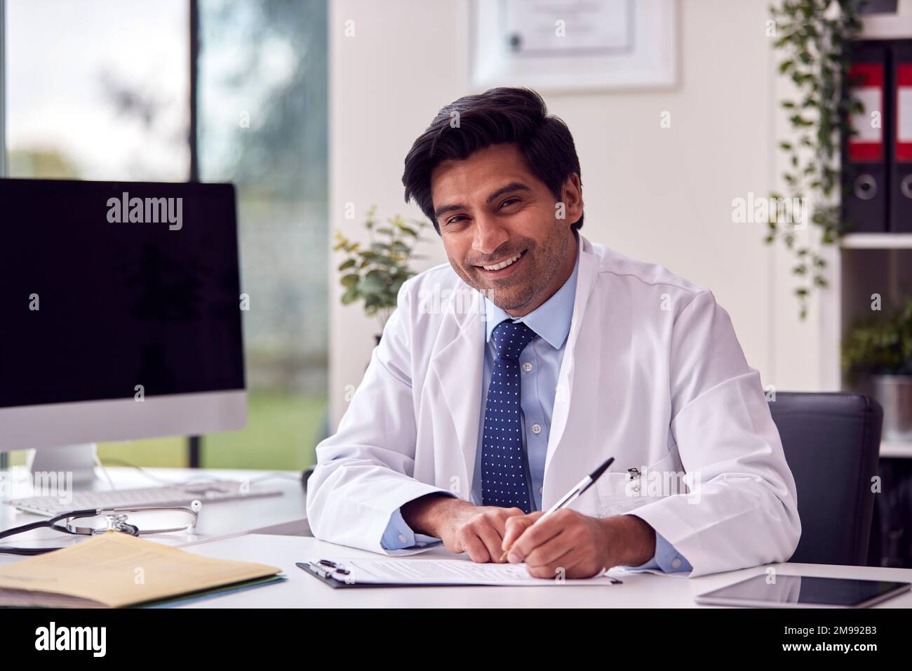 Portrait Of Male Doctor Or GP Wearing White Coat At Desk In Office ...