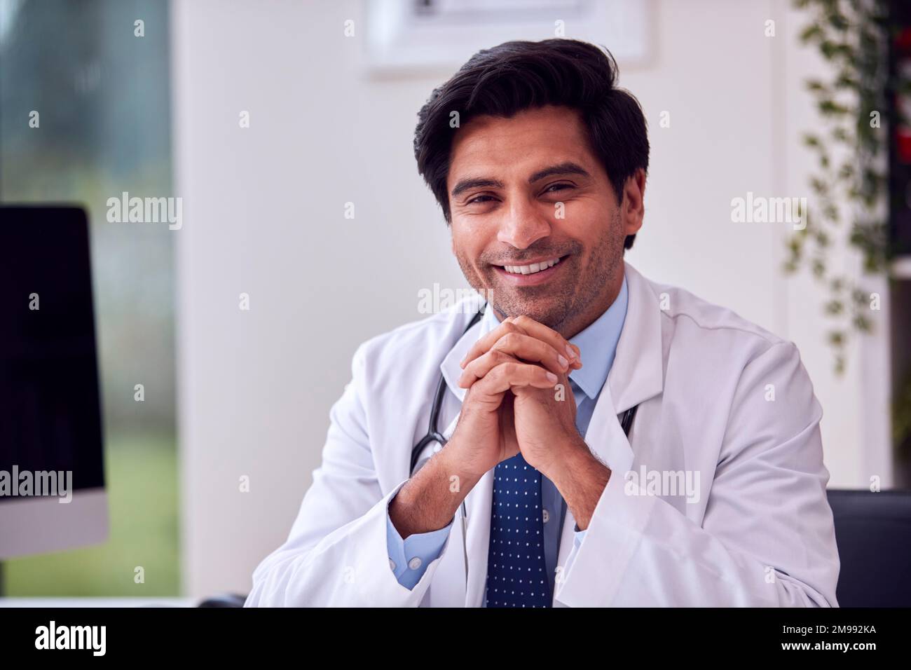 Portrait Of Male Doctor Or GP Wearing White Coat At Desk In Office ...