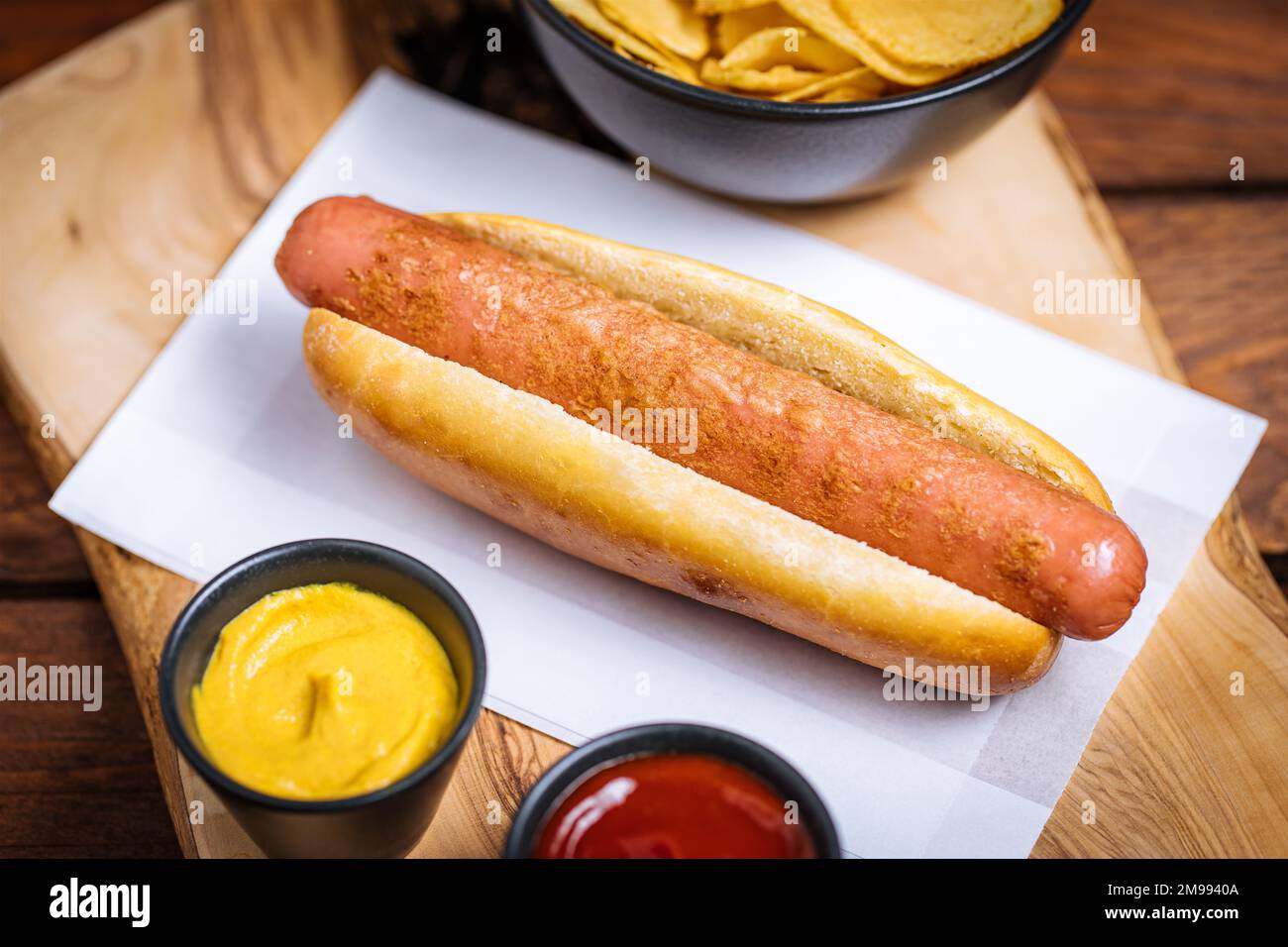 Classic fast food hot dog served with mustard on a rustic wooden board ...