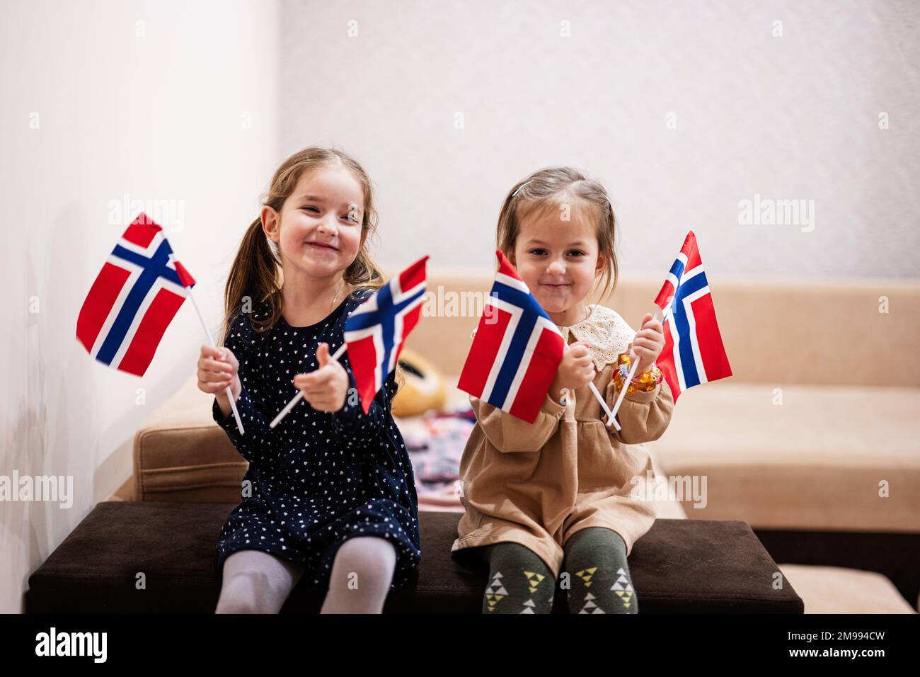 Two sisters are sitting on a couch at home with norwegian flags on ...