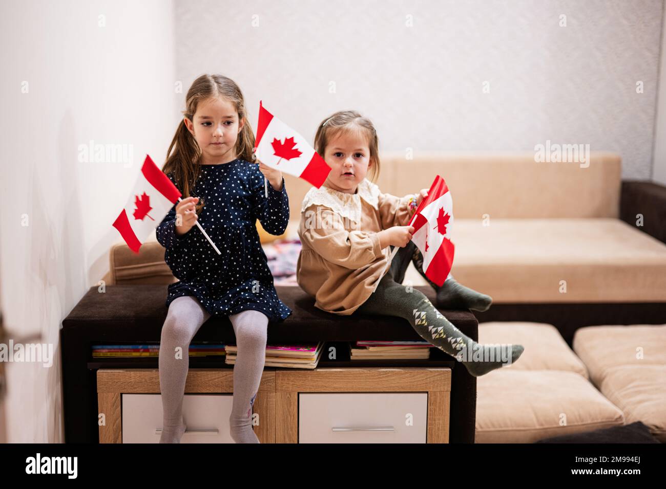 Two sisters are sitting on a couch at home with canadian flags on hands ...