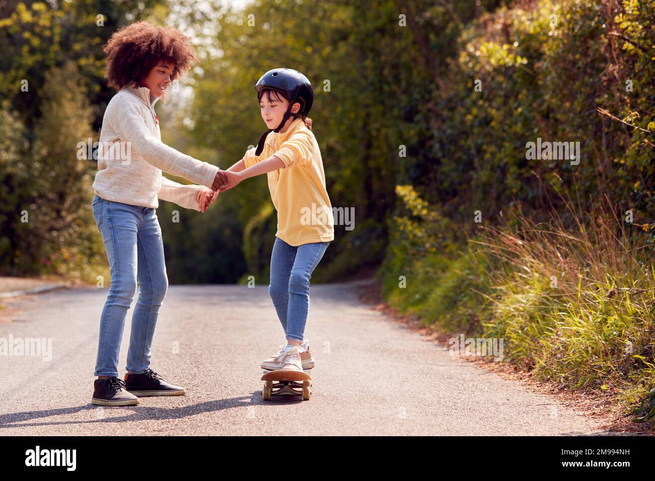 Boy Teaching Girl To Ride Skateboard Holding Her Hands On Country Road ...