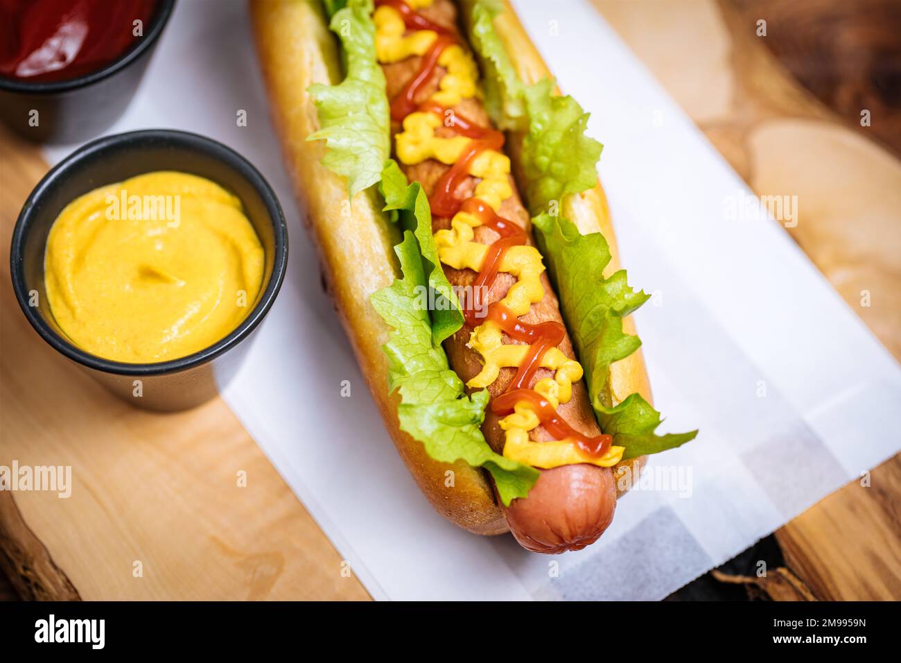 Hot dog with mustard, ketchup and green salad in bun, served with ...