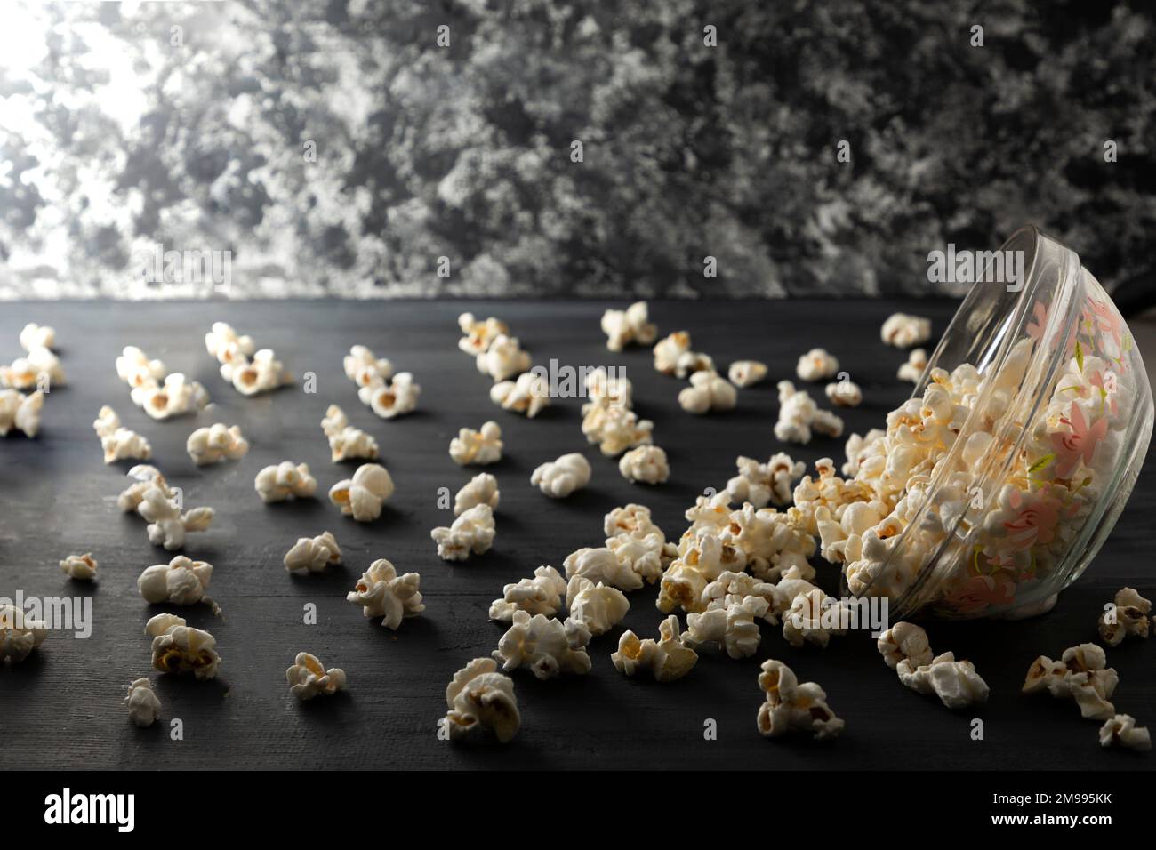 A bowl of popcorn lying on a black wooden base, with popcorn scattered ...