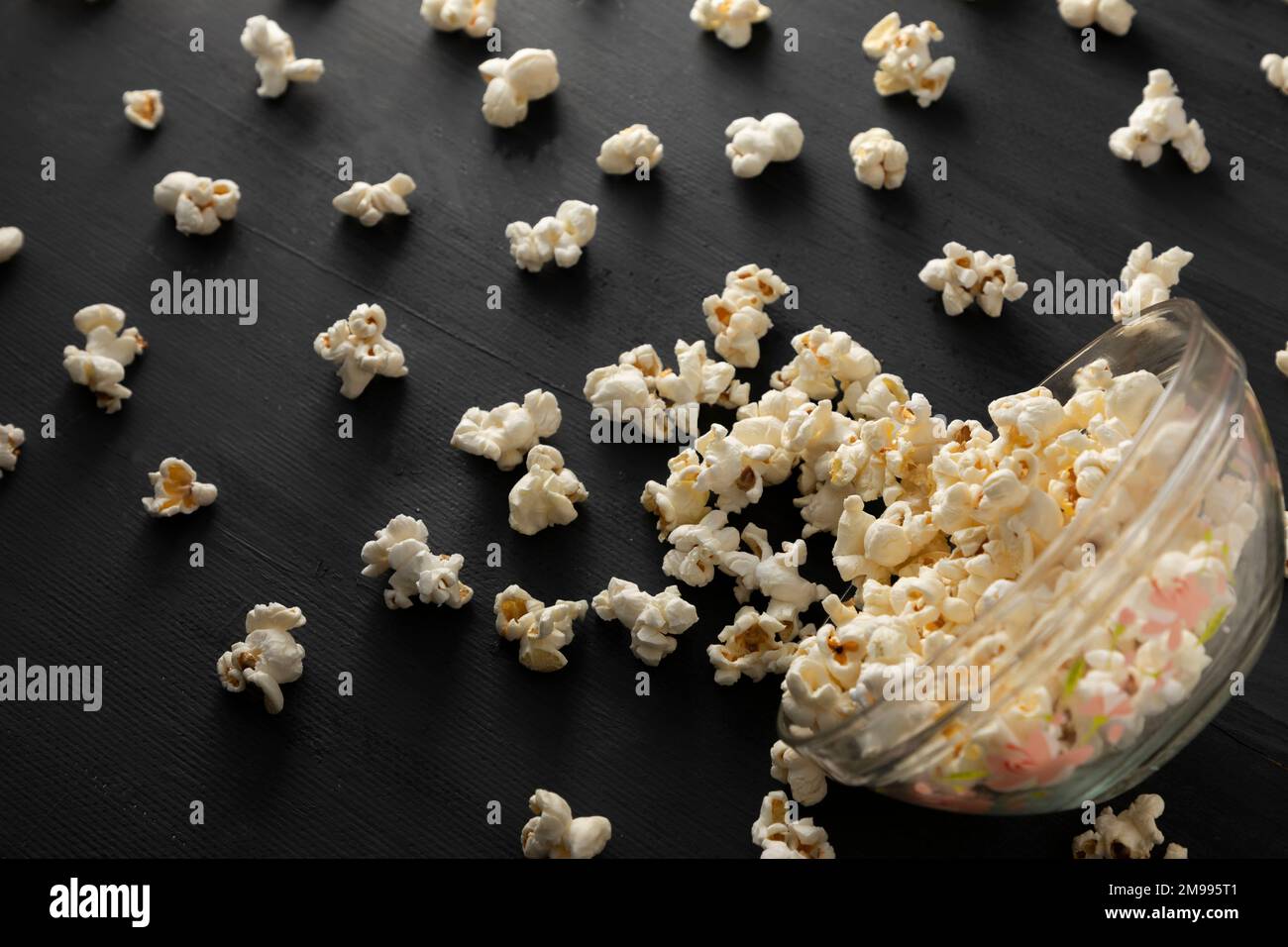 A bowl of popcorn lying on a black wooden base, with popcorn scattered ...
