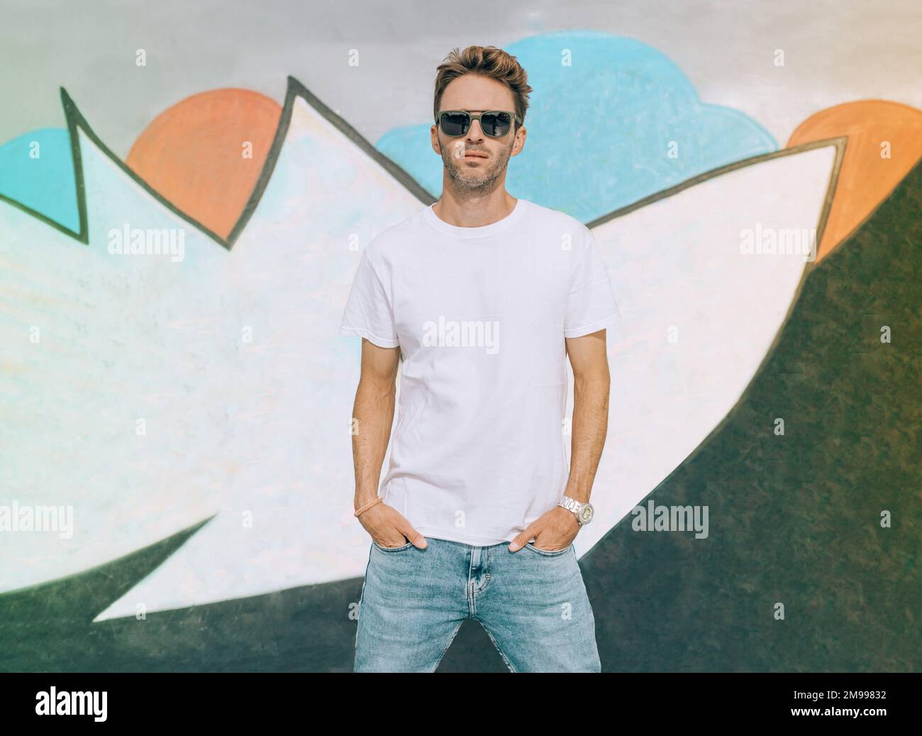 Young handsome guy is standing on a graffiti wall background. Man is ...