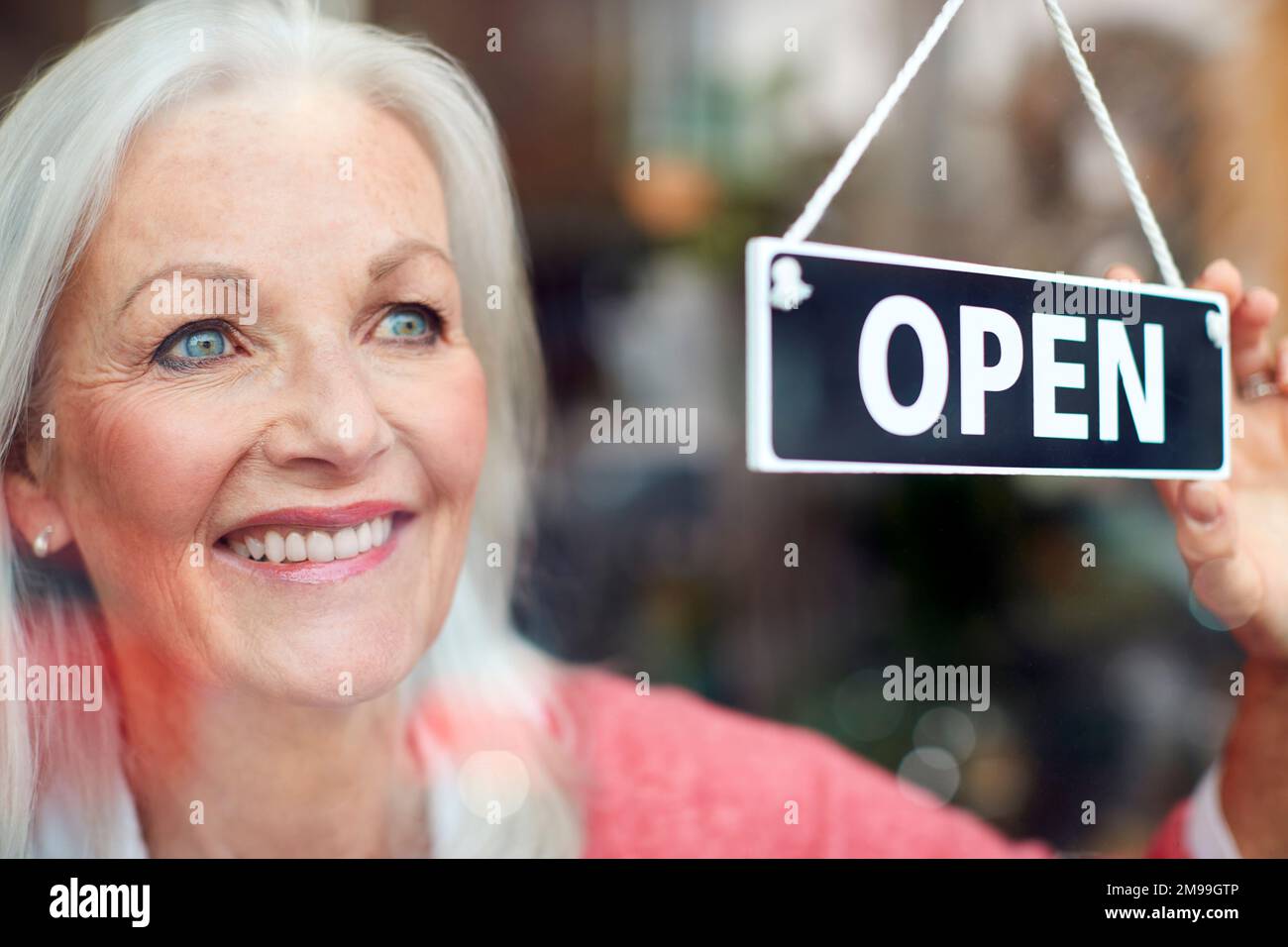 Smiling Female Owner Of Small Business Turning Round Open Sign In Shop ...