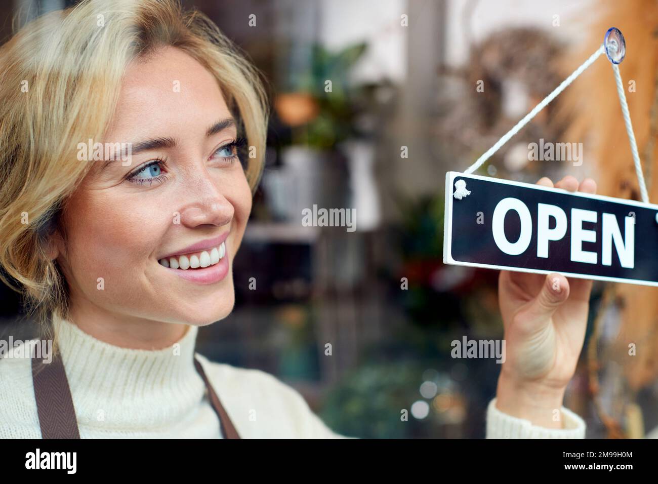 Smiling Female Owner Of Small Business Turning Round Open Sign In Shop ...