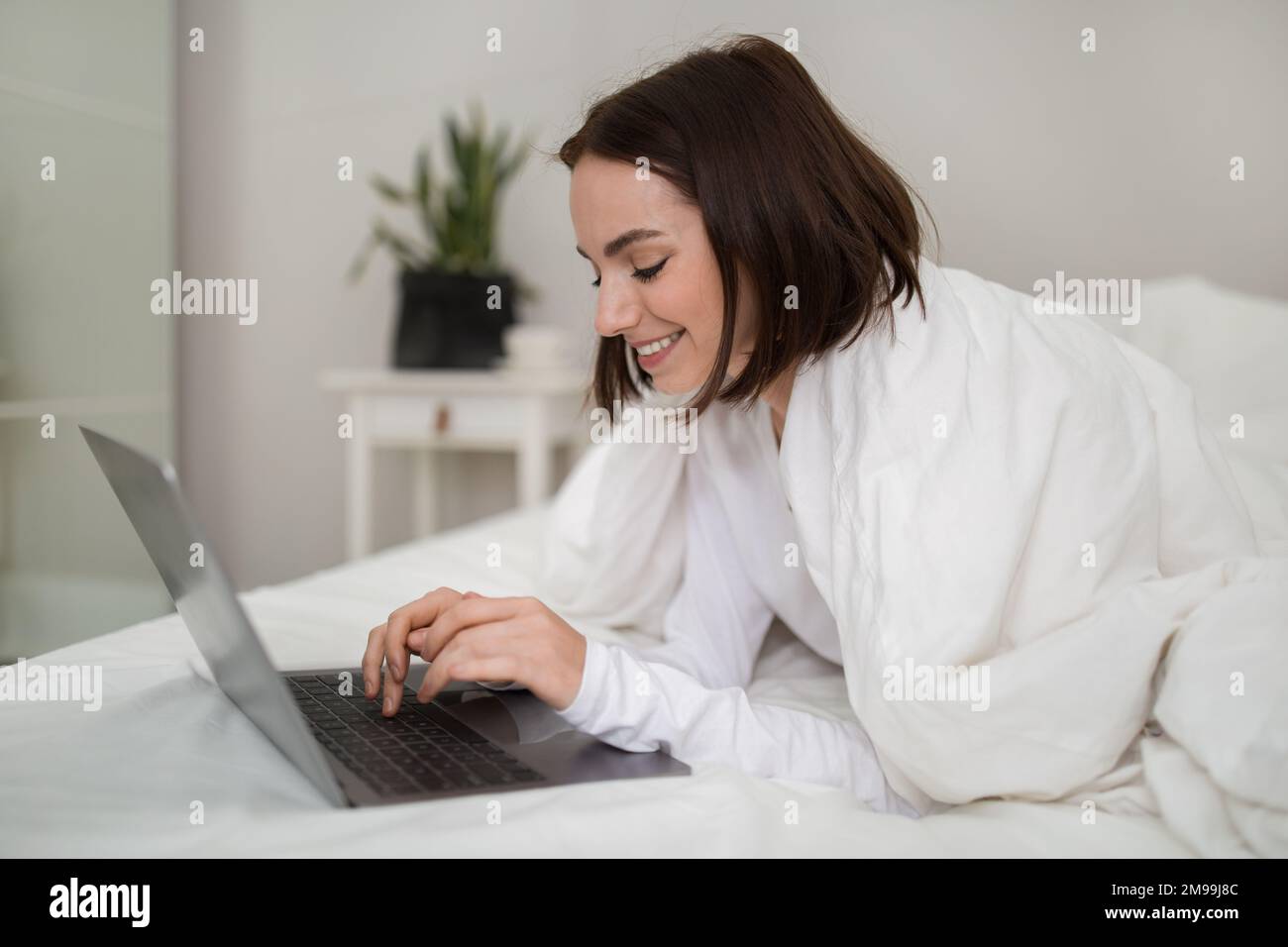 Relaxed young woman chilling in bed with modern laptop Stock Photo - Alamy