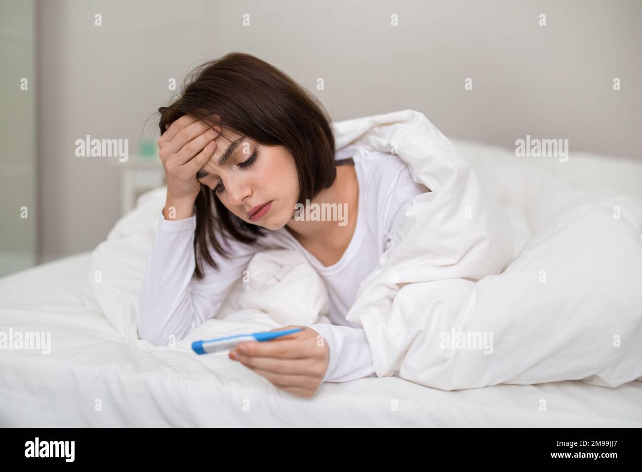 Upset woman checking fever while staying in bed at home Stock Photo - Alamy