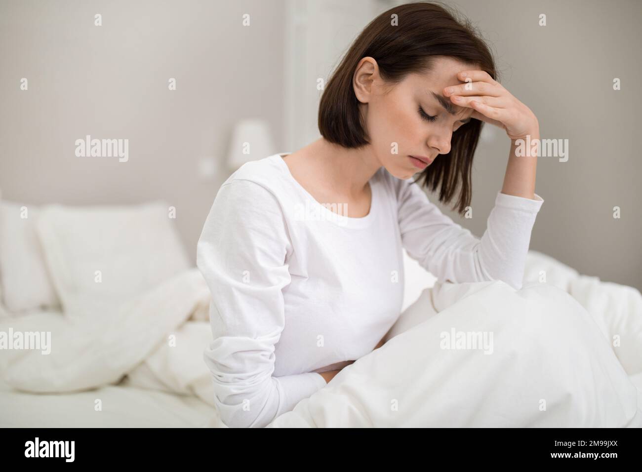Sick woman with headache sitting in bed Stock Photo - Alamy