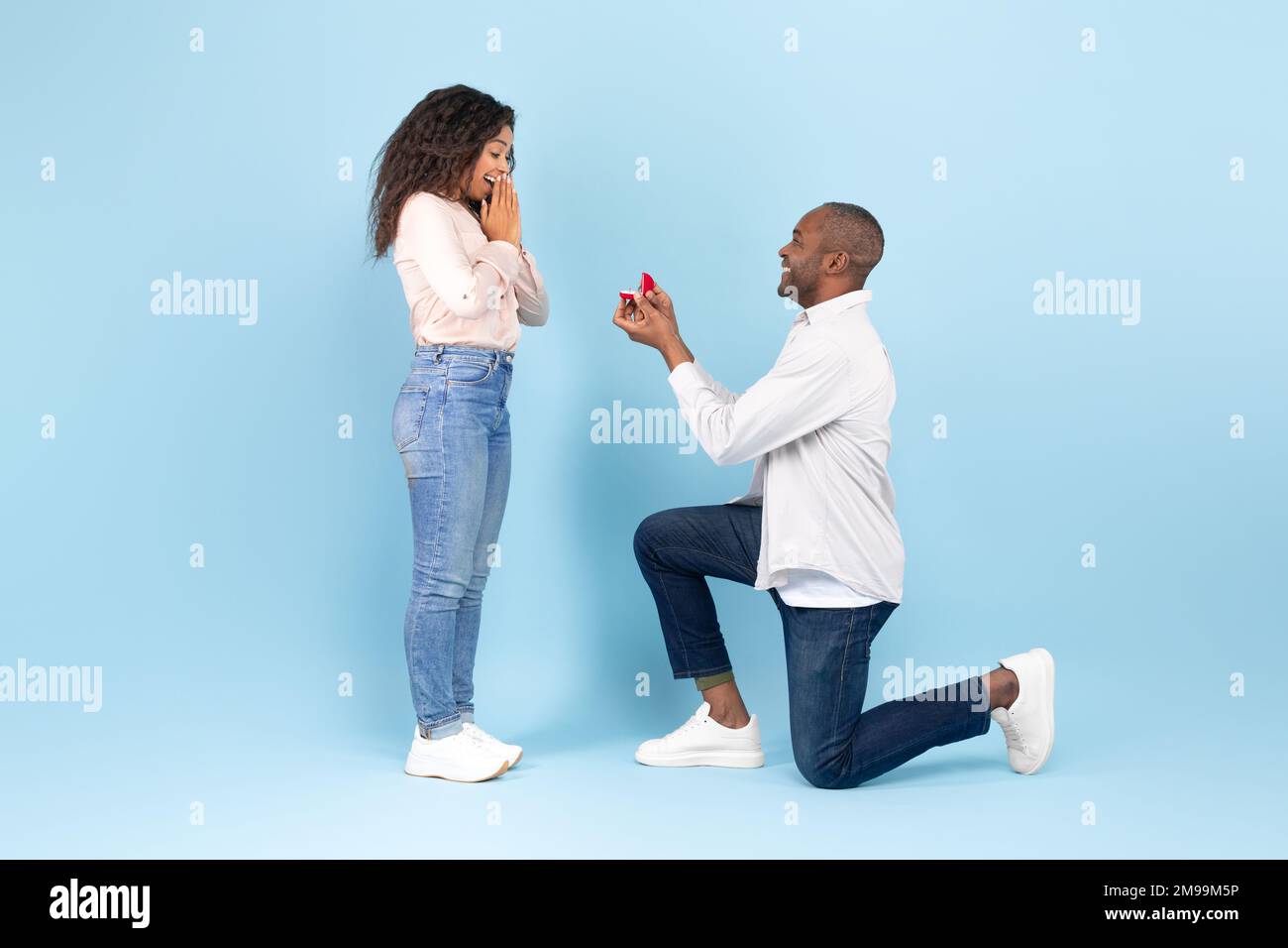 Loving black man standing on one knee and offering engagement ring to ...